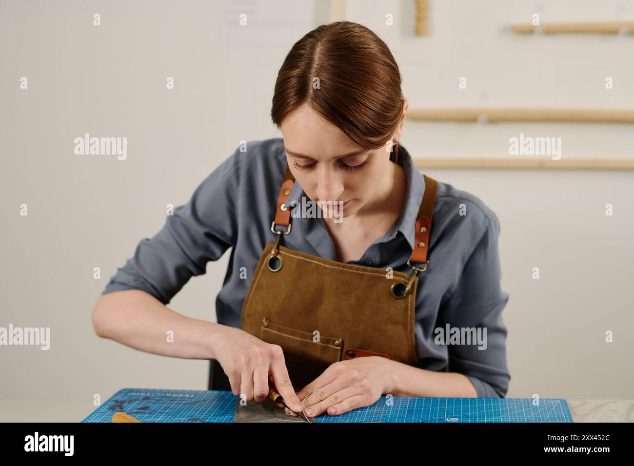 Young brunette craftswoman in workwear bending over workplace in studio ...
