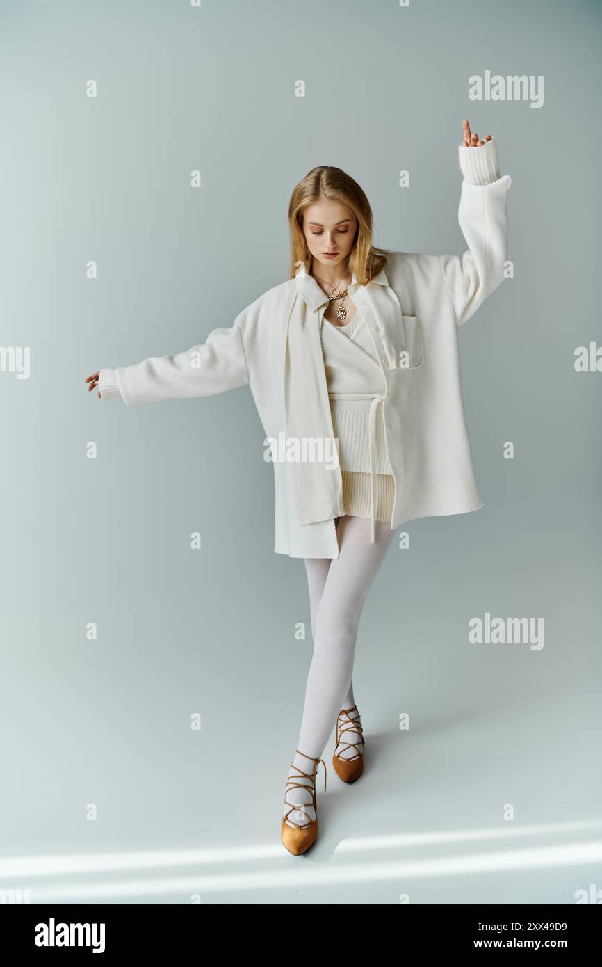 A young woman in a white outfit poses with one arm raised in a studio ...