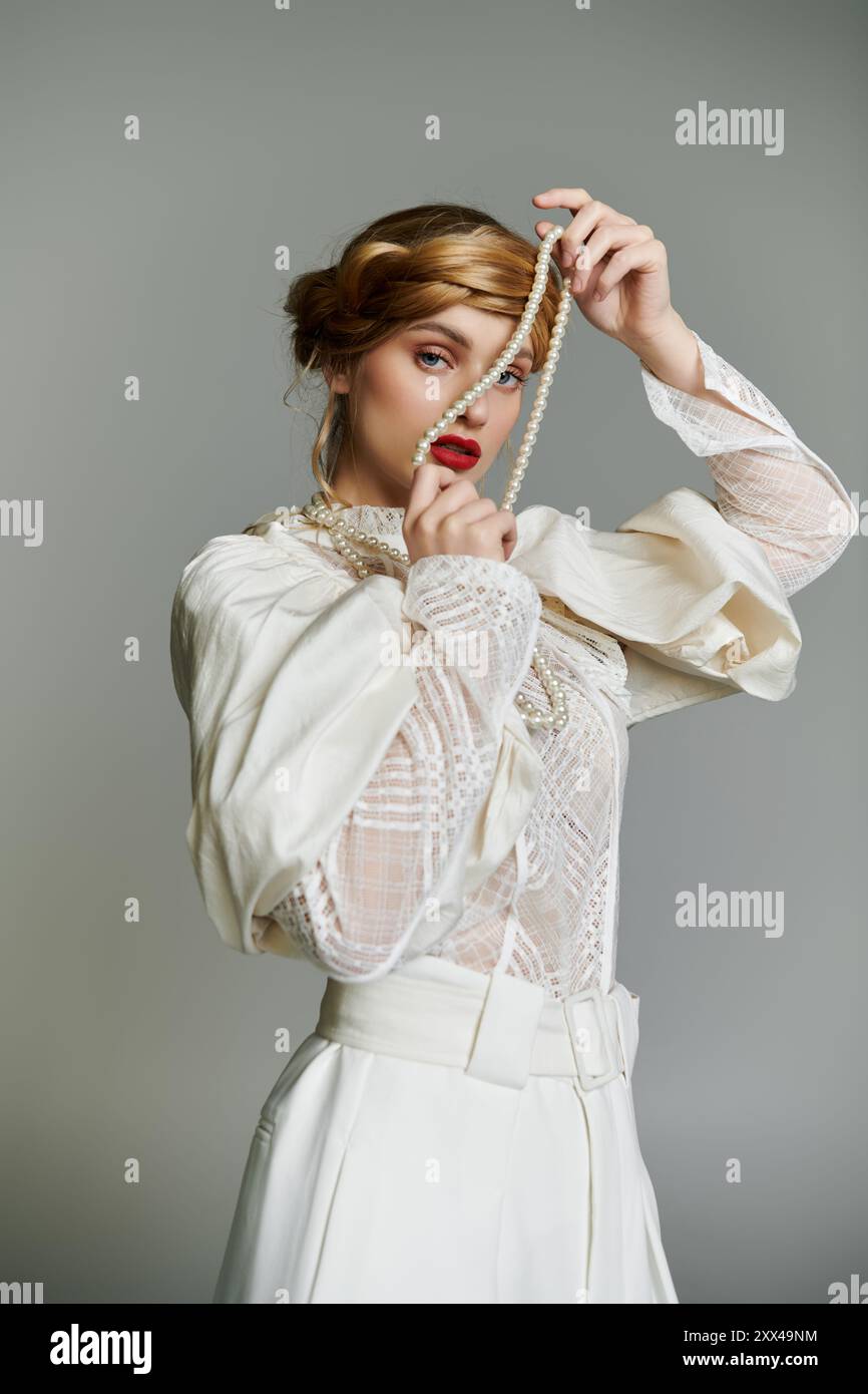 Woman in white lace top and pants poses with a pearl necklace over her ...