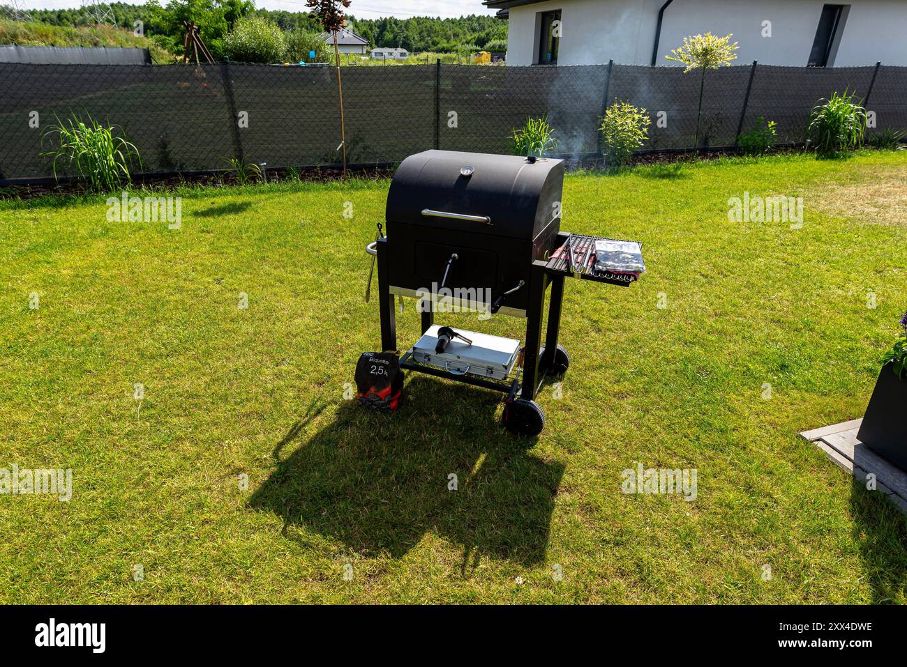 Smoke rising from a modern enclosed grill standing on a beautiful green ...