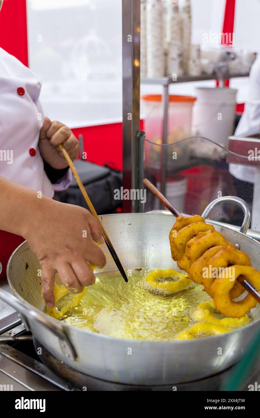 A woman is cooking picarones in a pan. The food is being cooked on a ...