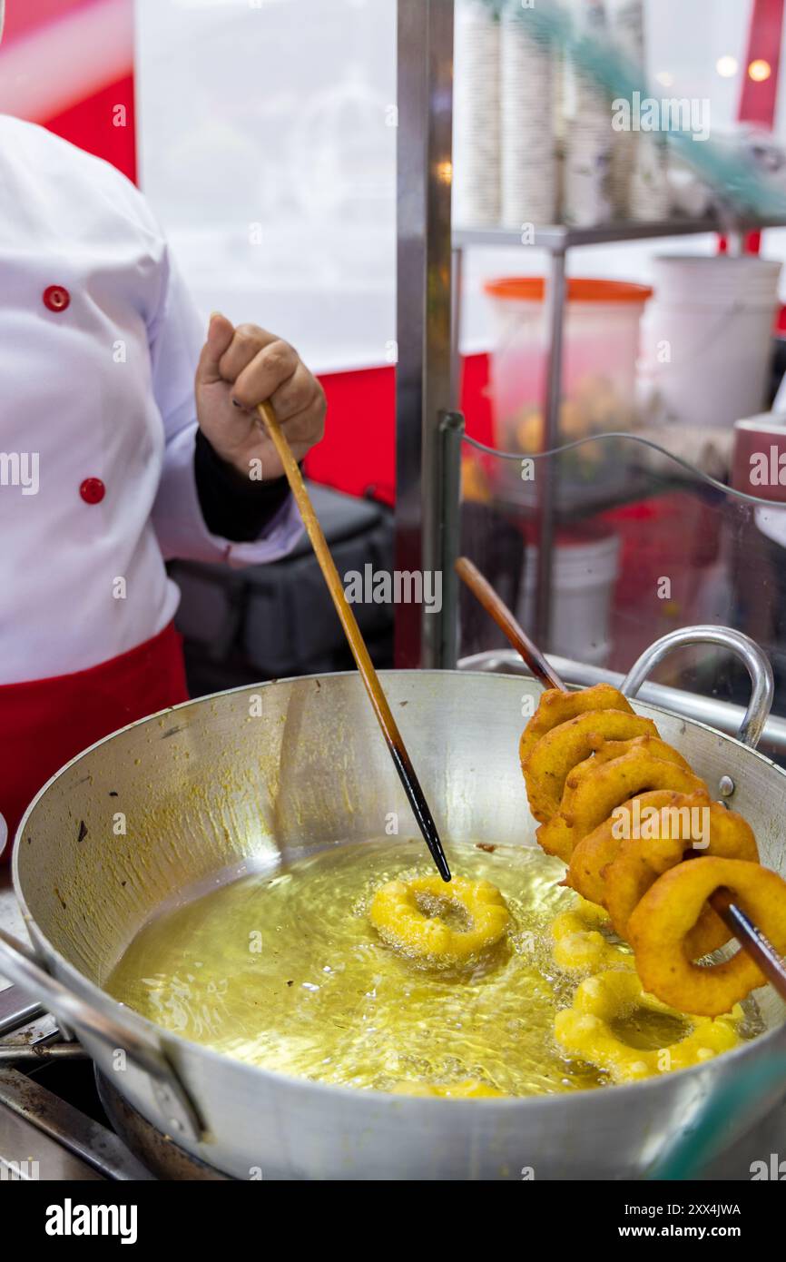 A woman is cooking picarones in a pan. The food is being cooked on a ...