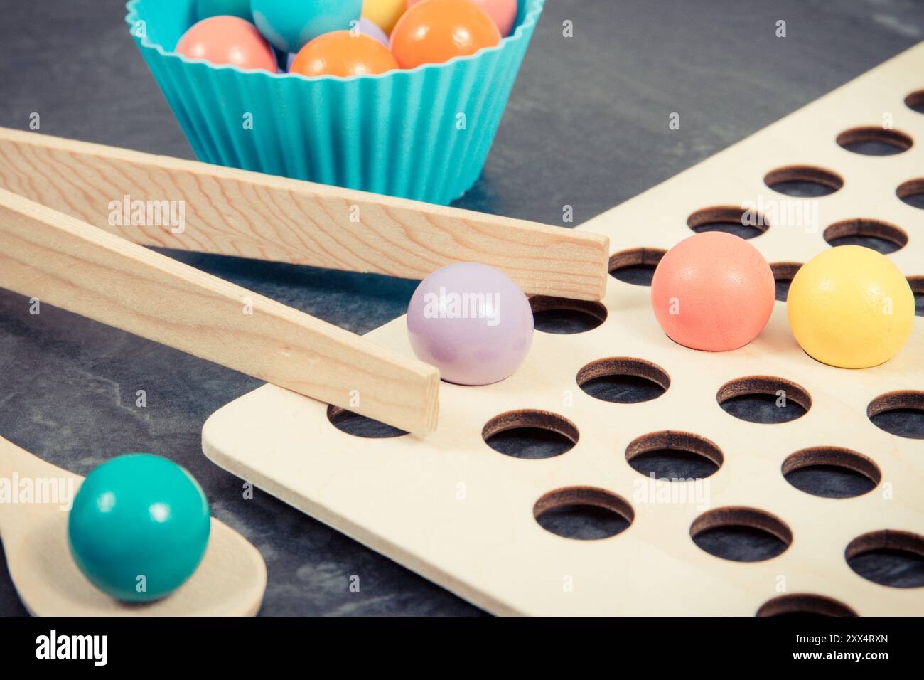 Small colorful balls with wooden spoon and tongs. Development of kids ...