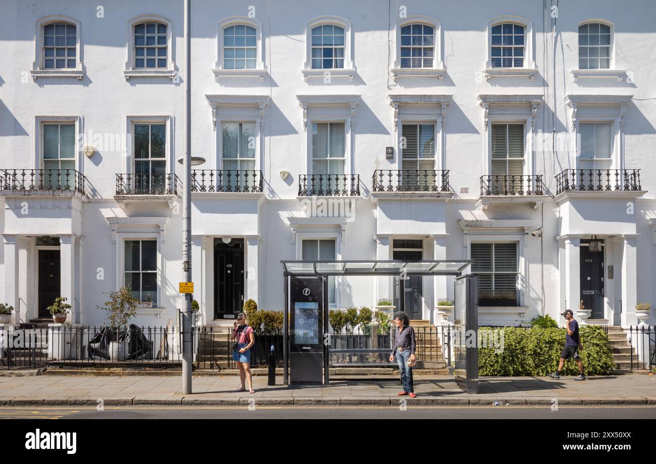 People wait at a bus stop outside a terrace of traditional townhouses ...