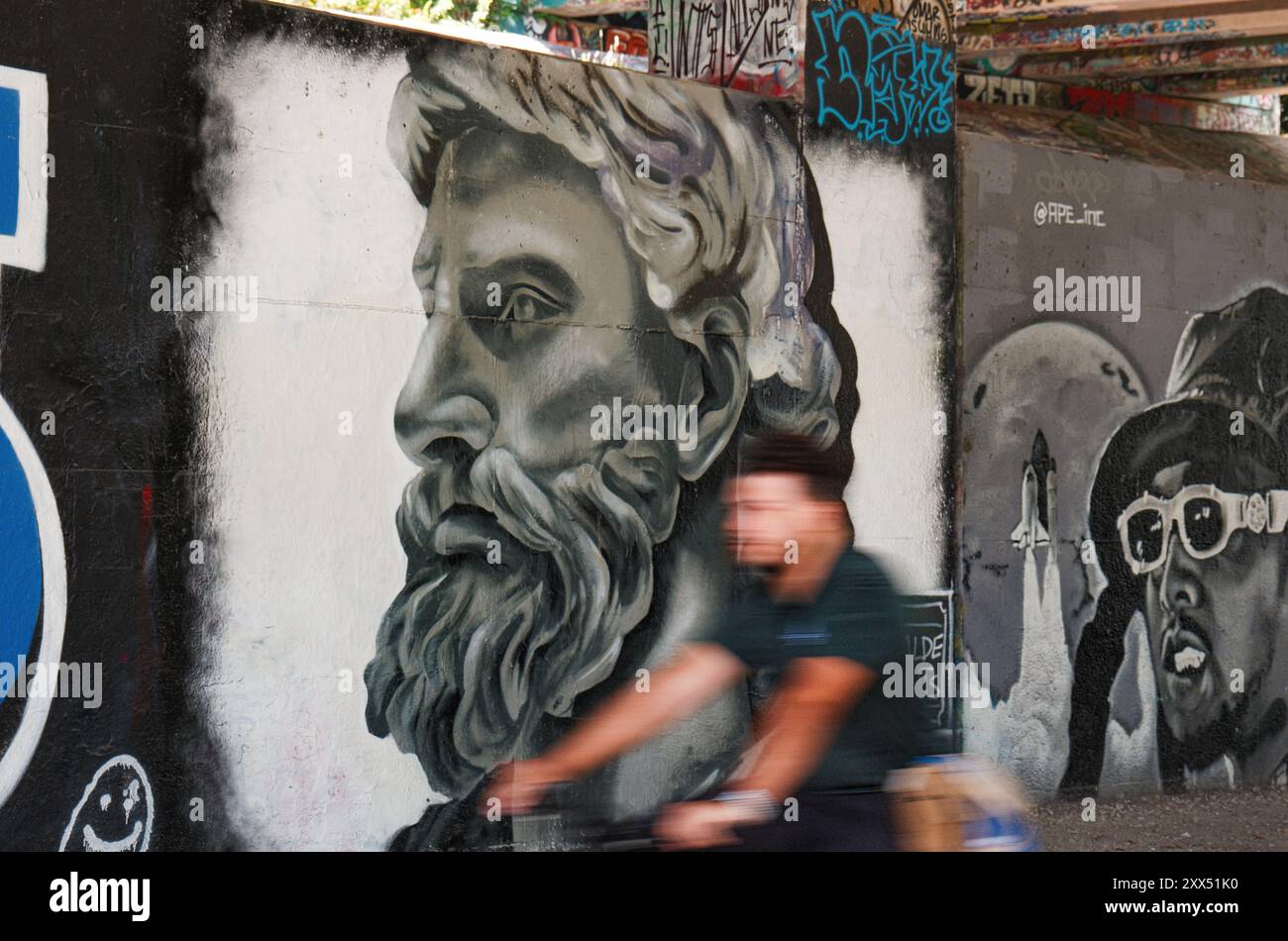 A biker rides speeds past graffiti underneath an bridge overpass on the ...