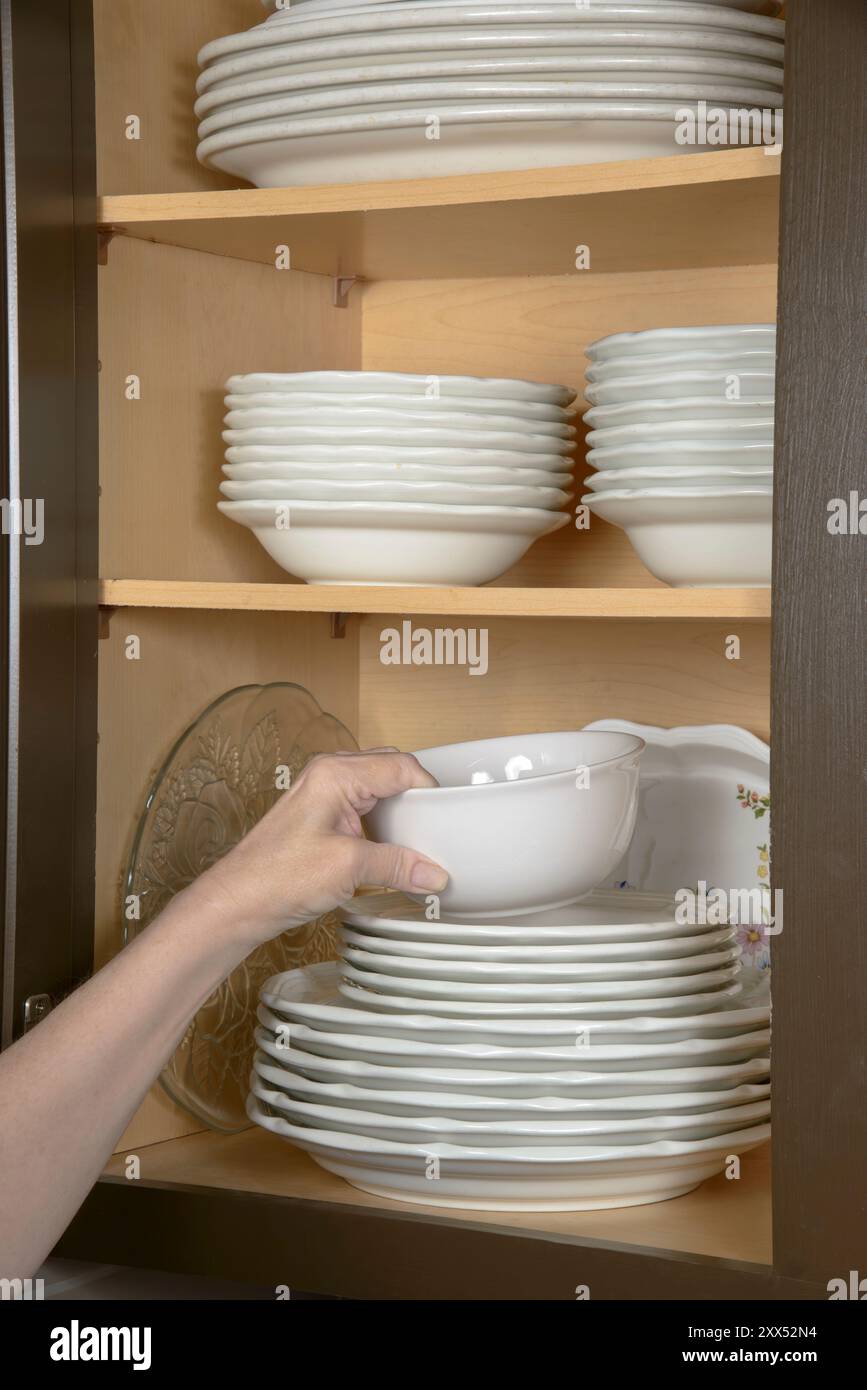 Vertical shot of a woman’s hand putting away dishes in a kitchen ...