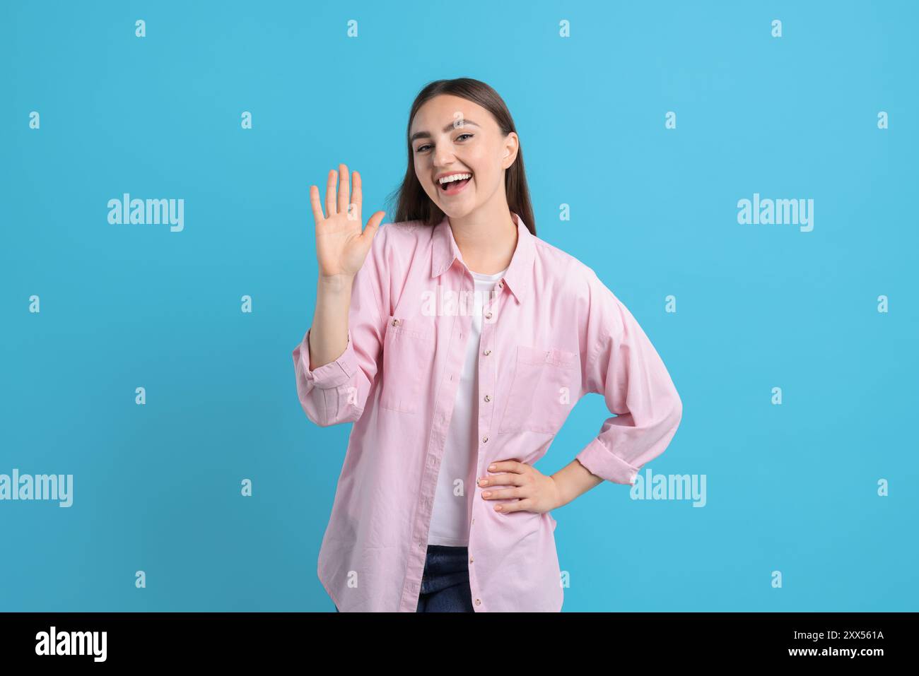 Happy woman waving on light blue background Stock Photo - Alamy