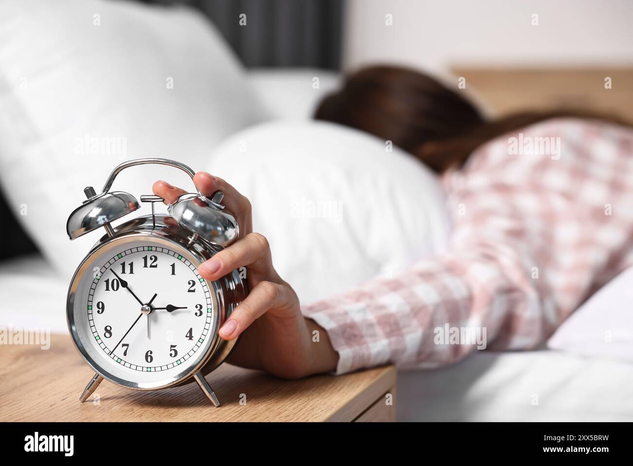 Woman turning off alarm clock in bedroom at lunch time, selective focus ...