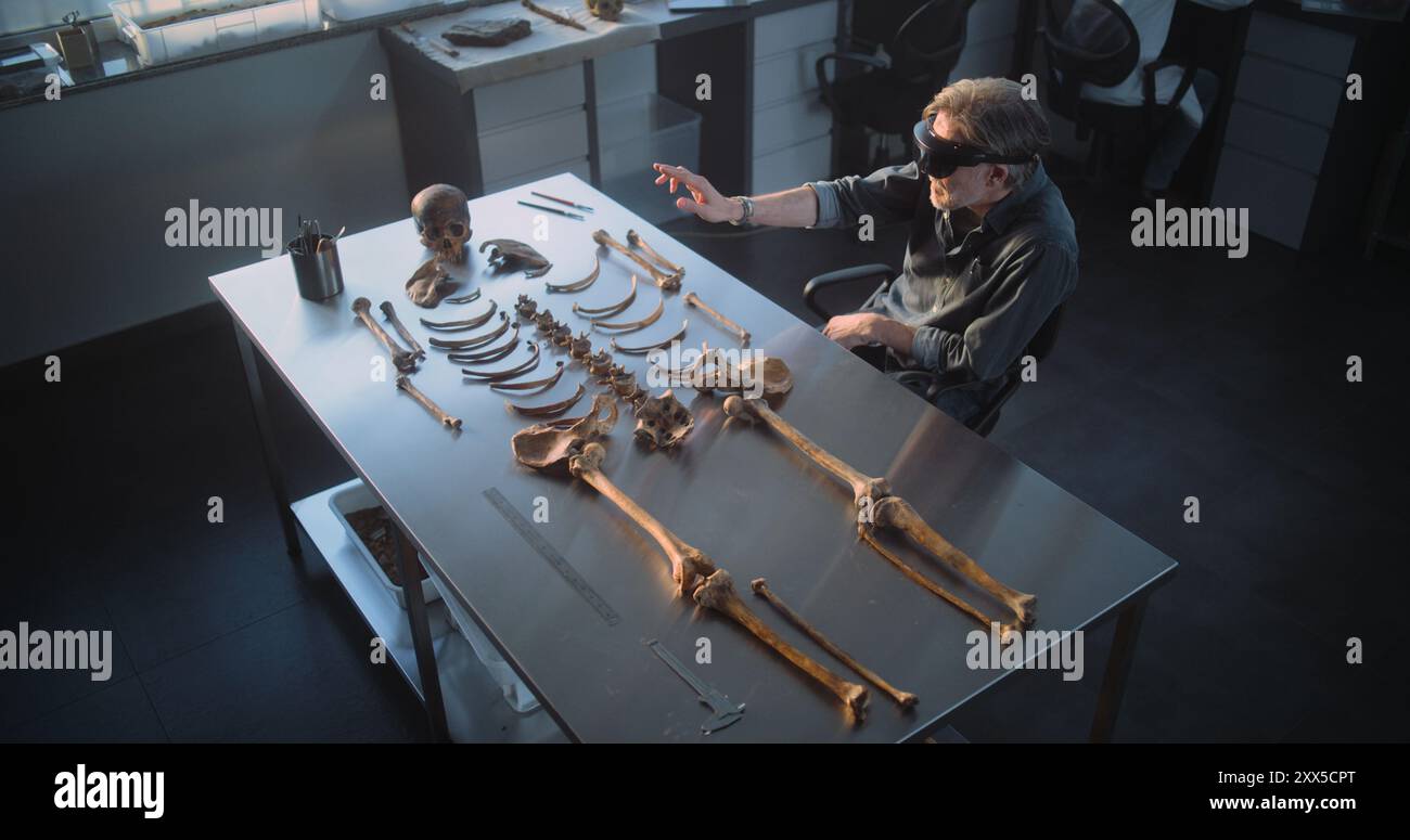Mature archaeologist in VR headset studies remains of ancient extinct human skeleton using ...