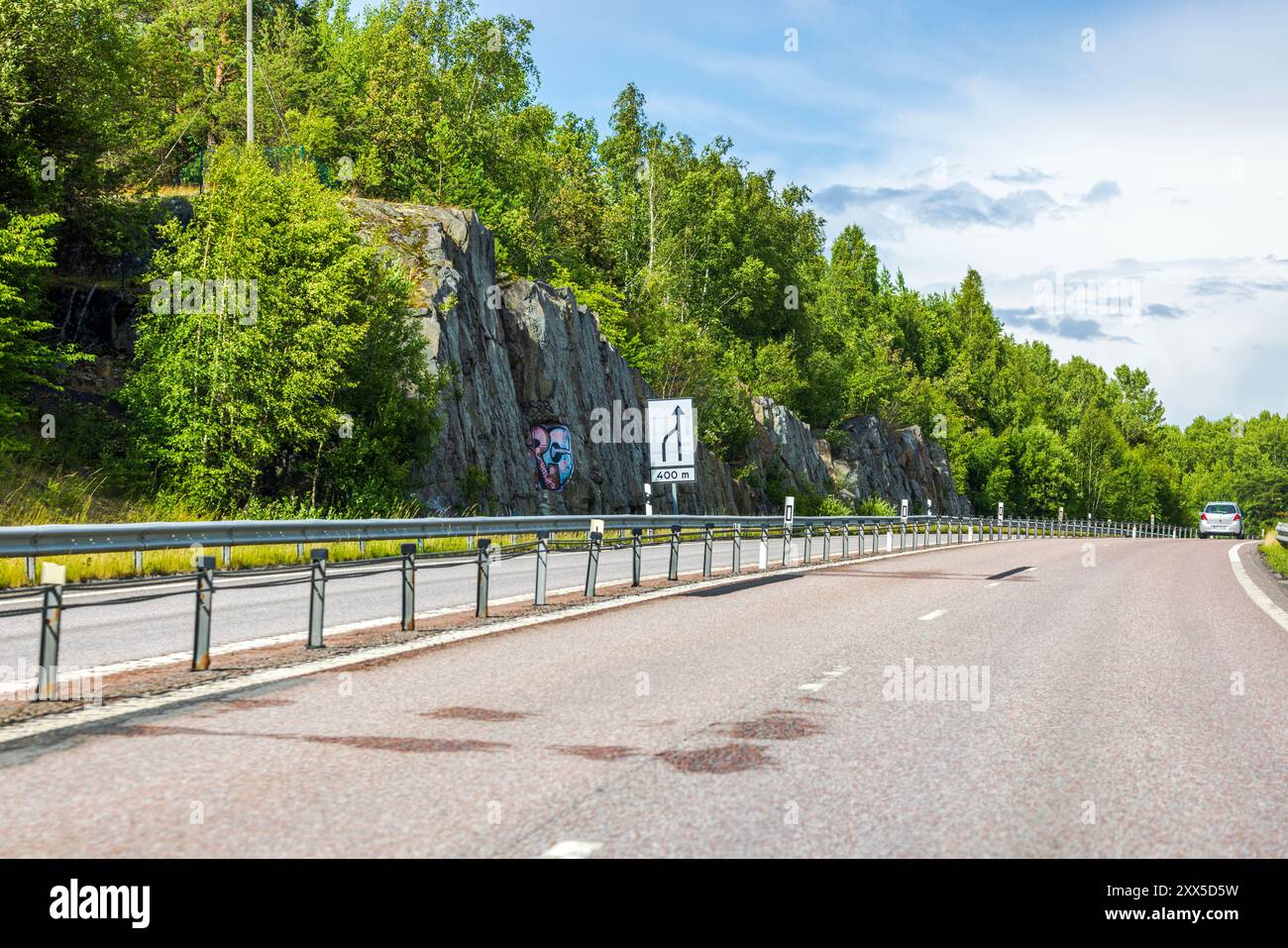 Highway with road narrowing sign against backdrop of rocky mountains ...