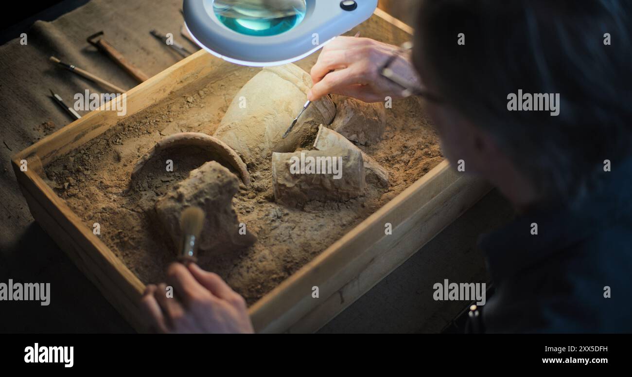 Close up of mature archaeologist cleaning cultural heritage of extinct civilization from sand ...