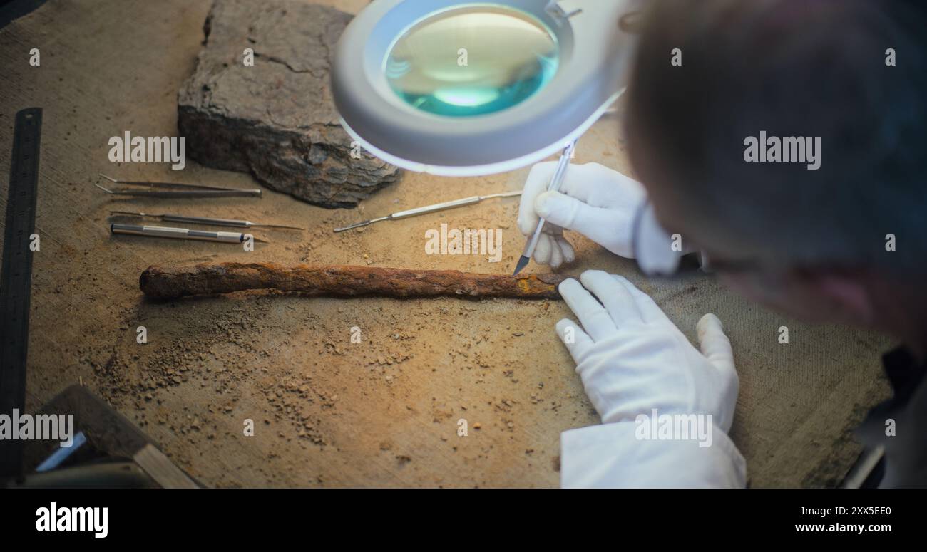 Senior archaeologist cleans fossil ancient wooden spear under lamp using professional tools ...