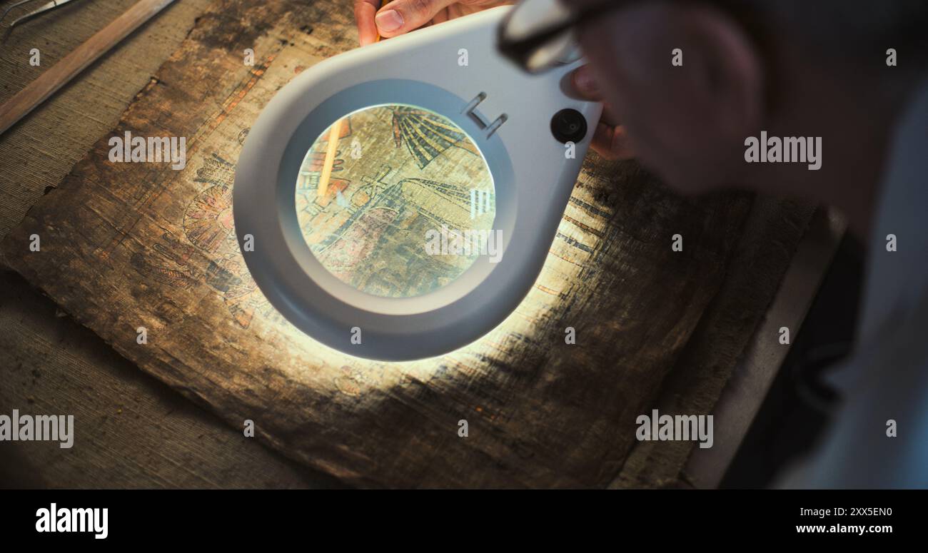 Senior archaeologist looks through magnifying lamp, studies ancient ...