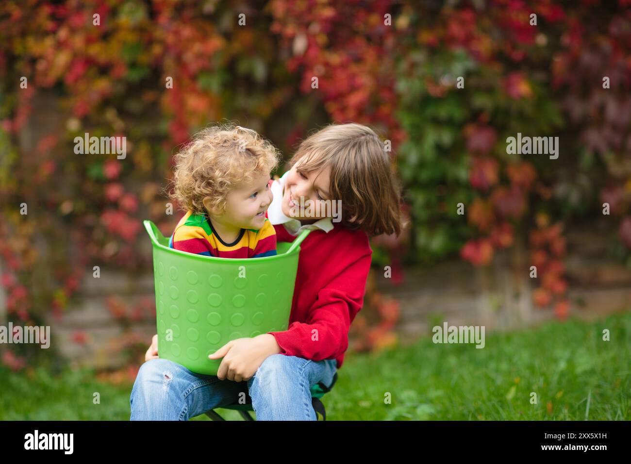 Kids play in autumn park. Children throwing yellow and red leaves ...