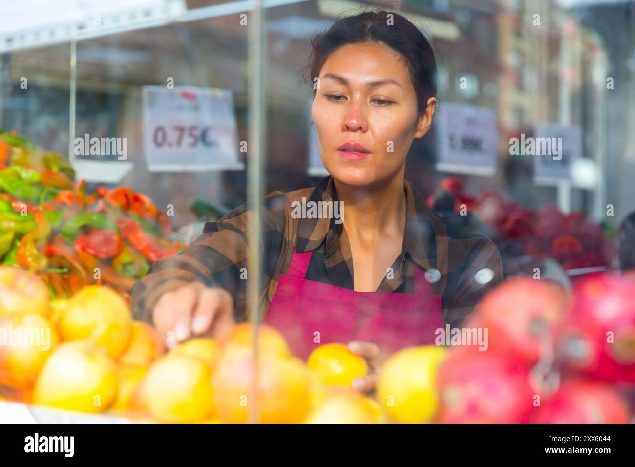 View behind glass of female seller laying out fruits and vegetables on ...