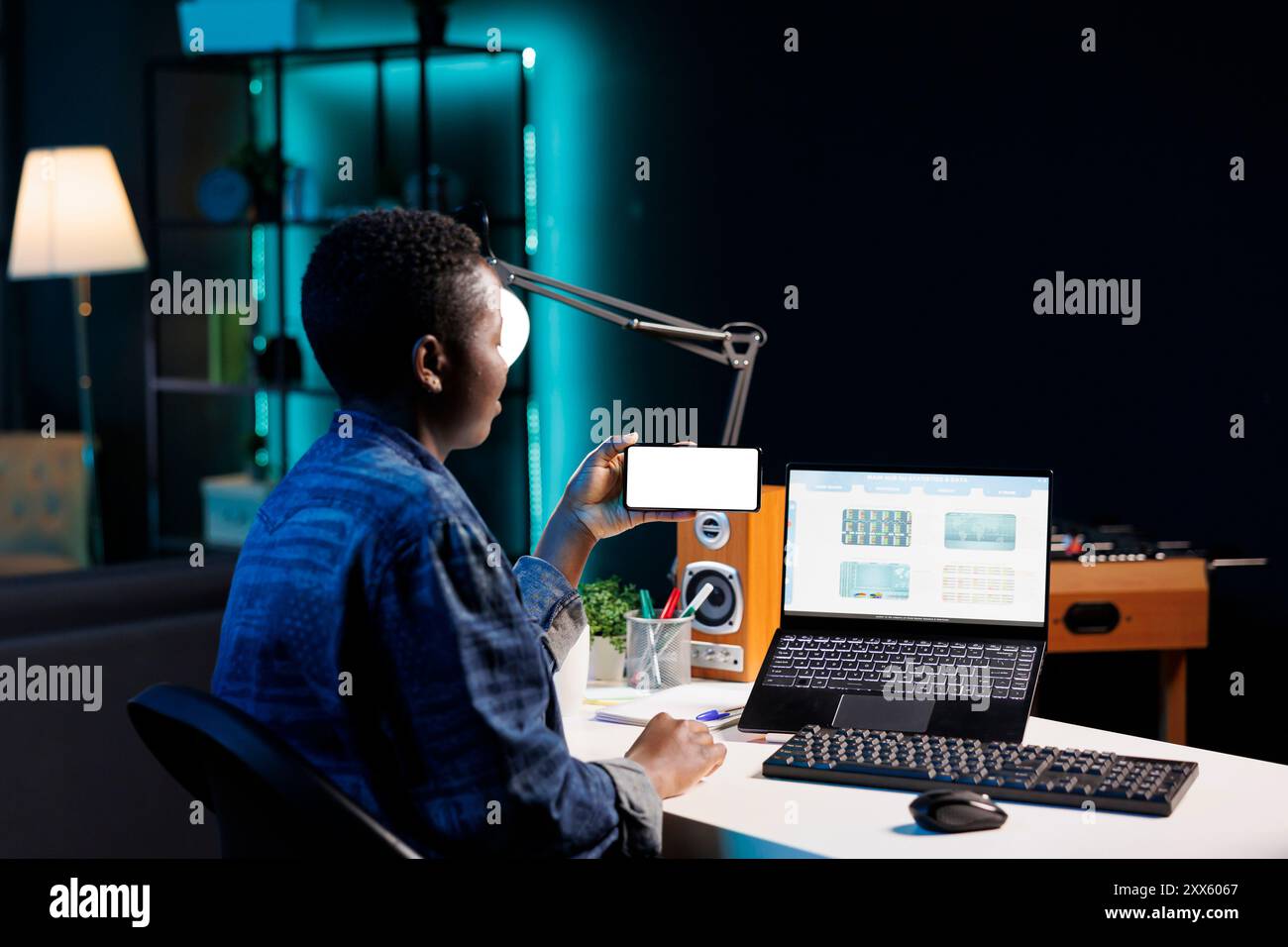 Female freelancer holding smartphone with white screen and using laptop ...