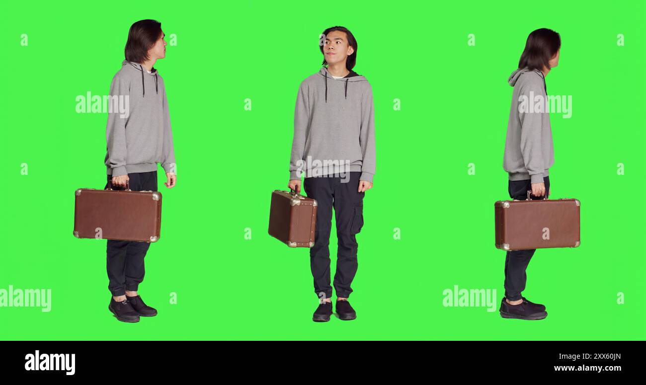 Young adult carries retro suitcase over full body greenscreen backdrop ...