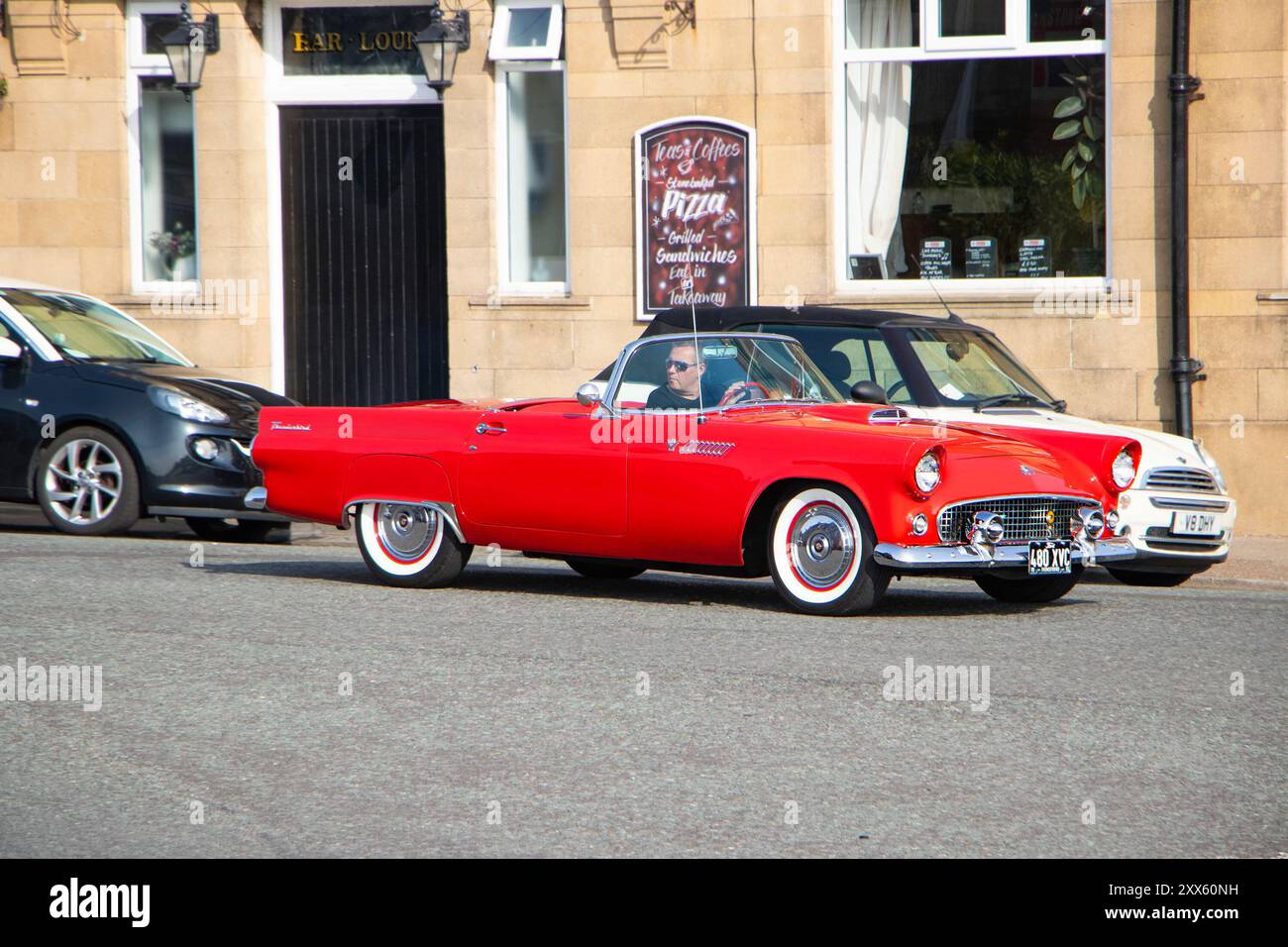 A classic red convertible ford thunderbird car driving down a street ...
