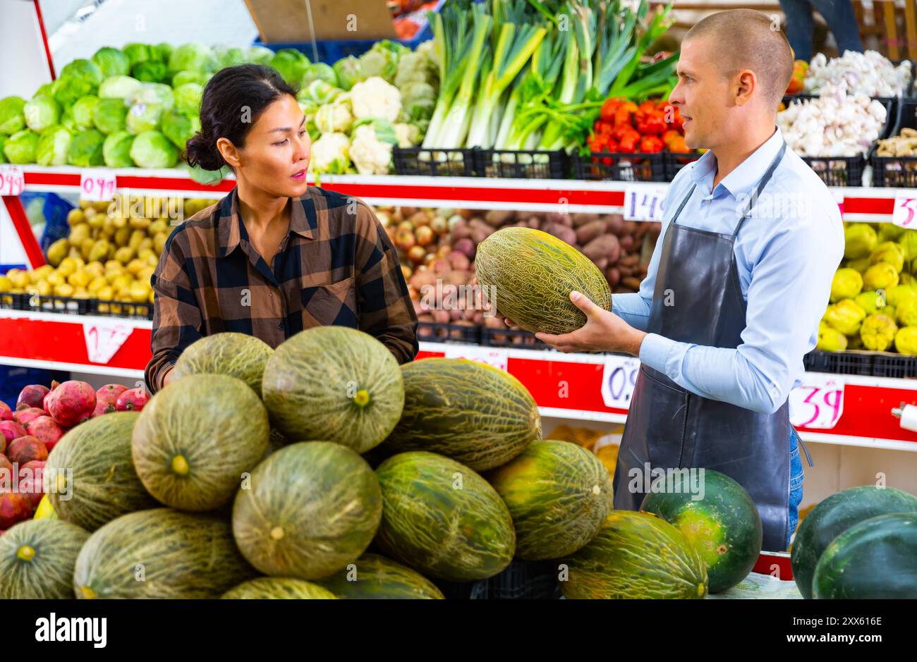 Salesman helping female shopper choose melon in shop Stock Photo - Alamy
