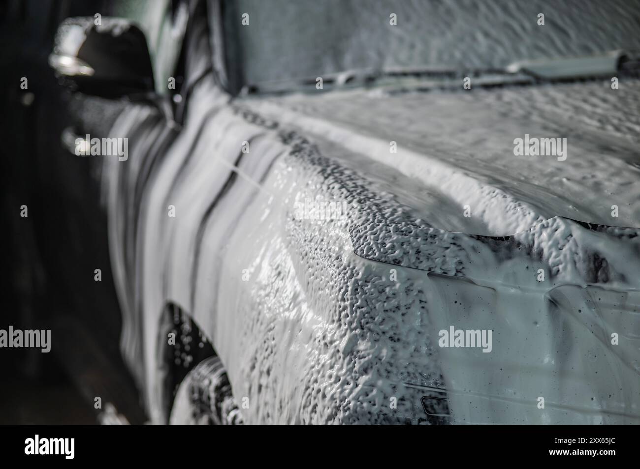 Foam drips from the bumper of a black car. Car wash Stock Photo - Alamy