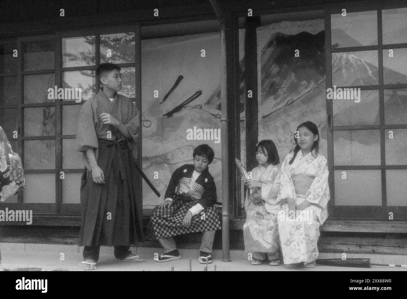 A group dressed in kimono and hakama poses outside a traditional home ...