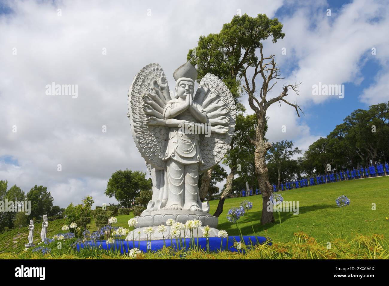 A stone angel statue with wings, surrounded by trees and flowers under ...