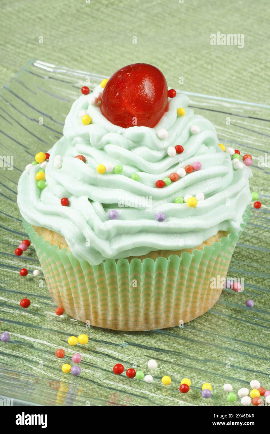 Close-up of a cupcake with green buttercream icing, rainbow sugar sprinkles and candied cherry ...