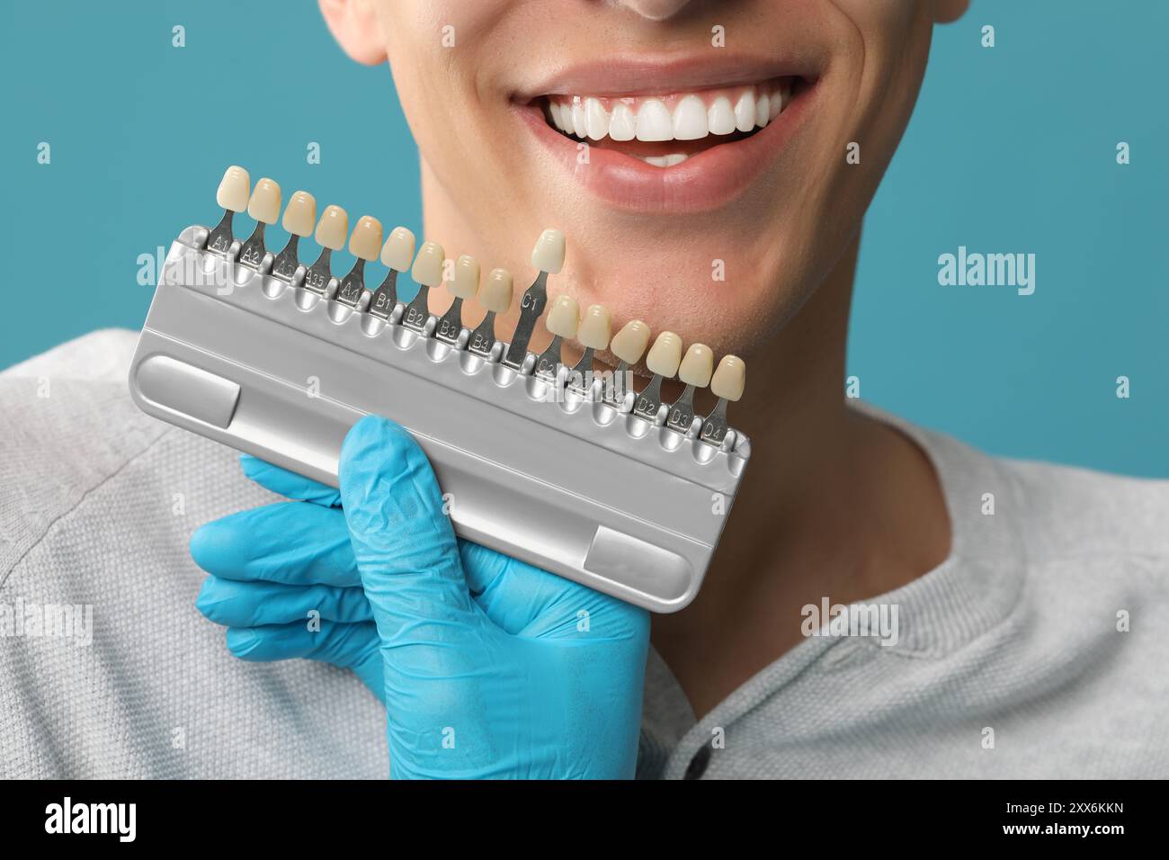 Doctor checking young man's teeth color on light blue background ...