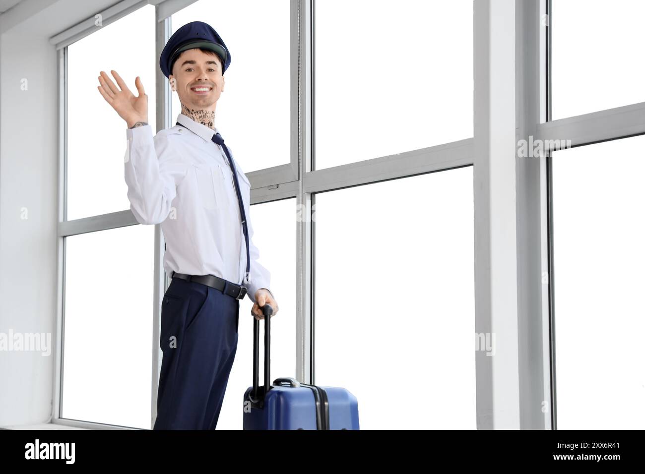 Male pilot with suitcase waving hand near window at airport Stock Photo ...
