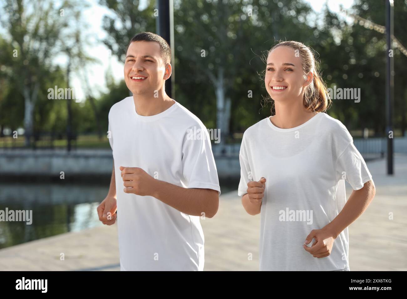 Sporty young woman jogging with personal trainer along waterfront ...