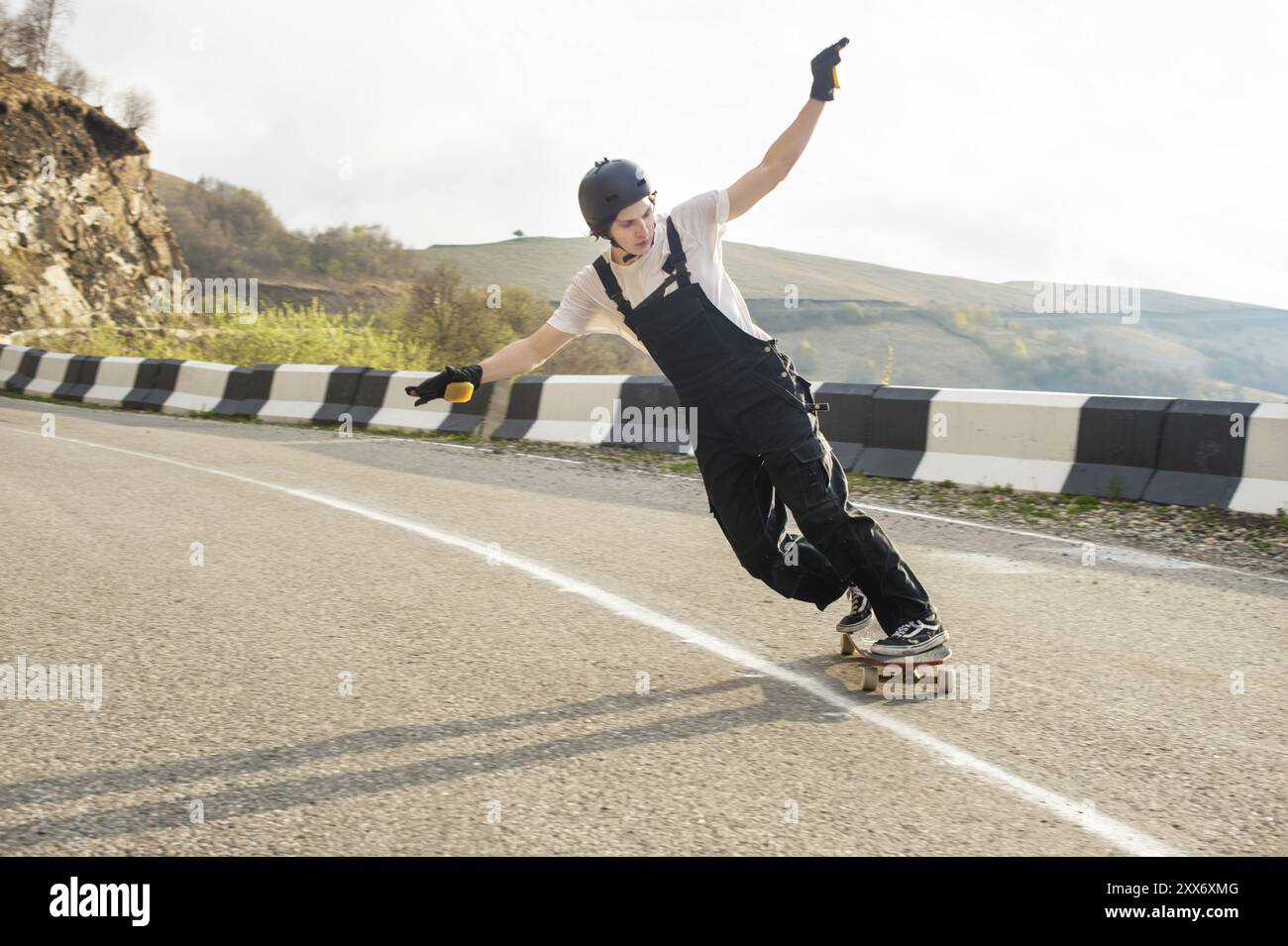 A young rider on a longboard in a helmet and gloves overall performs a ...