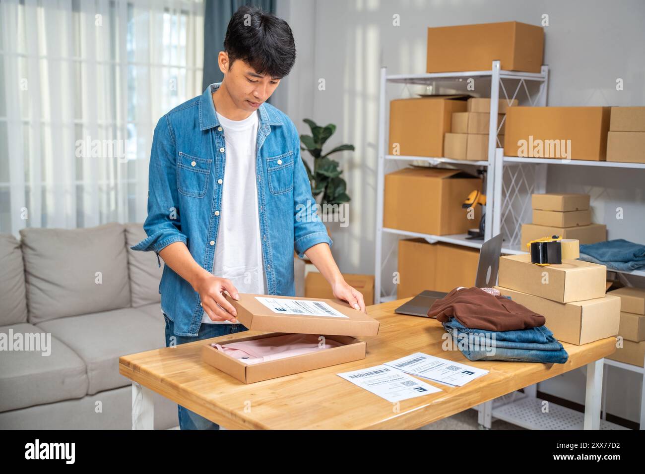 Young online seller man packing his shirt product in the box to ship to ...