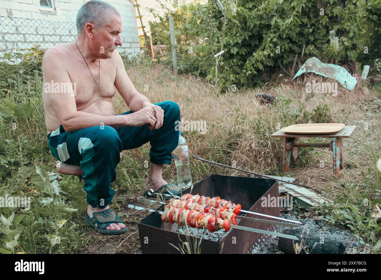 Senior man sitting on chair in garden with grill. Old man on the ...