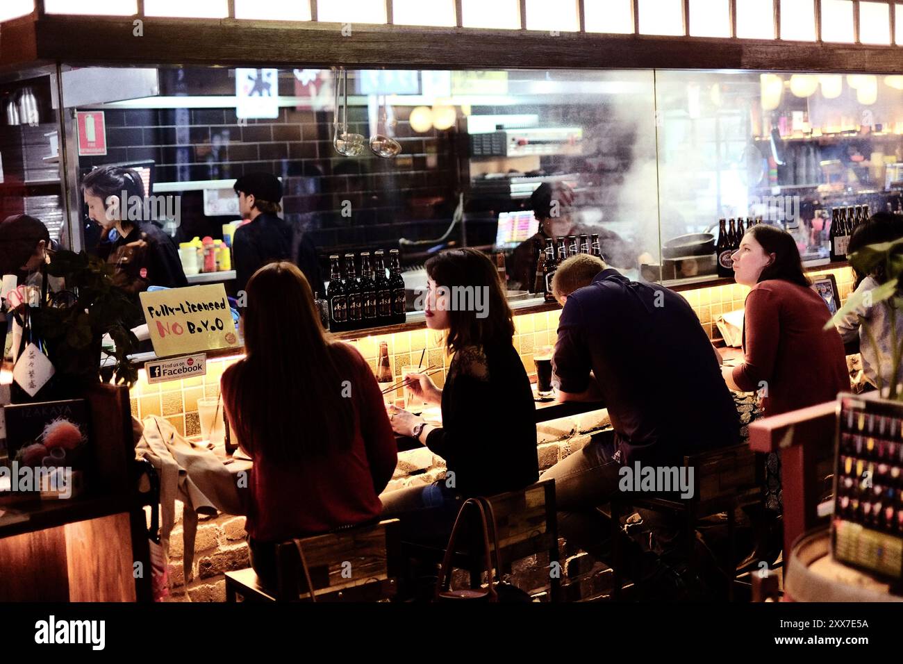 People eating at the counter of a steamy Japanese food bar and diner in ...