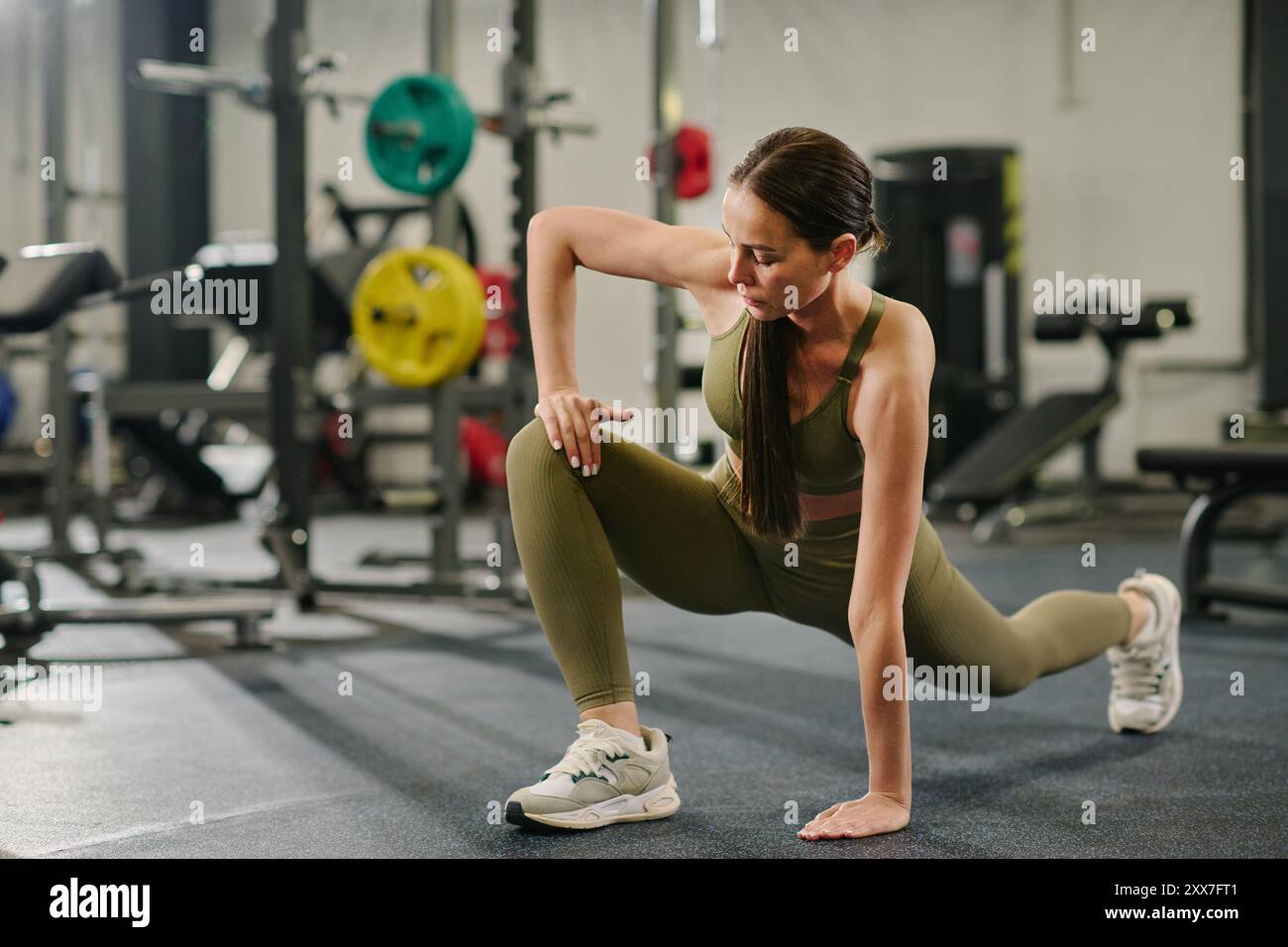 Toned female athlete practicing static stretching in fully equipped gym ...