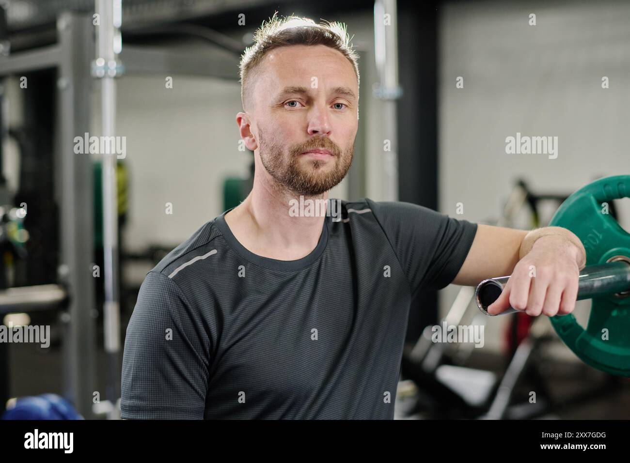 Portrait of brutal gym resident leaning on dumbbell while having break ...
