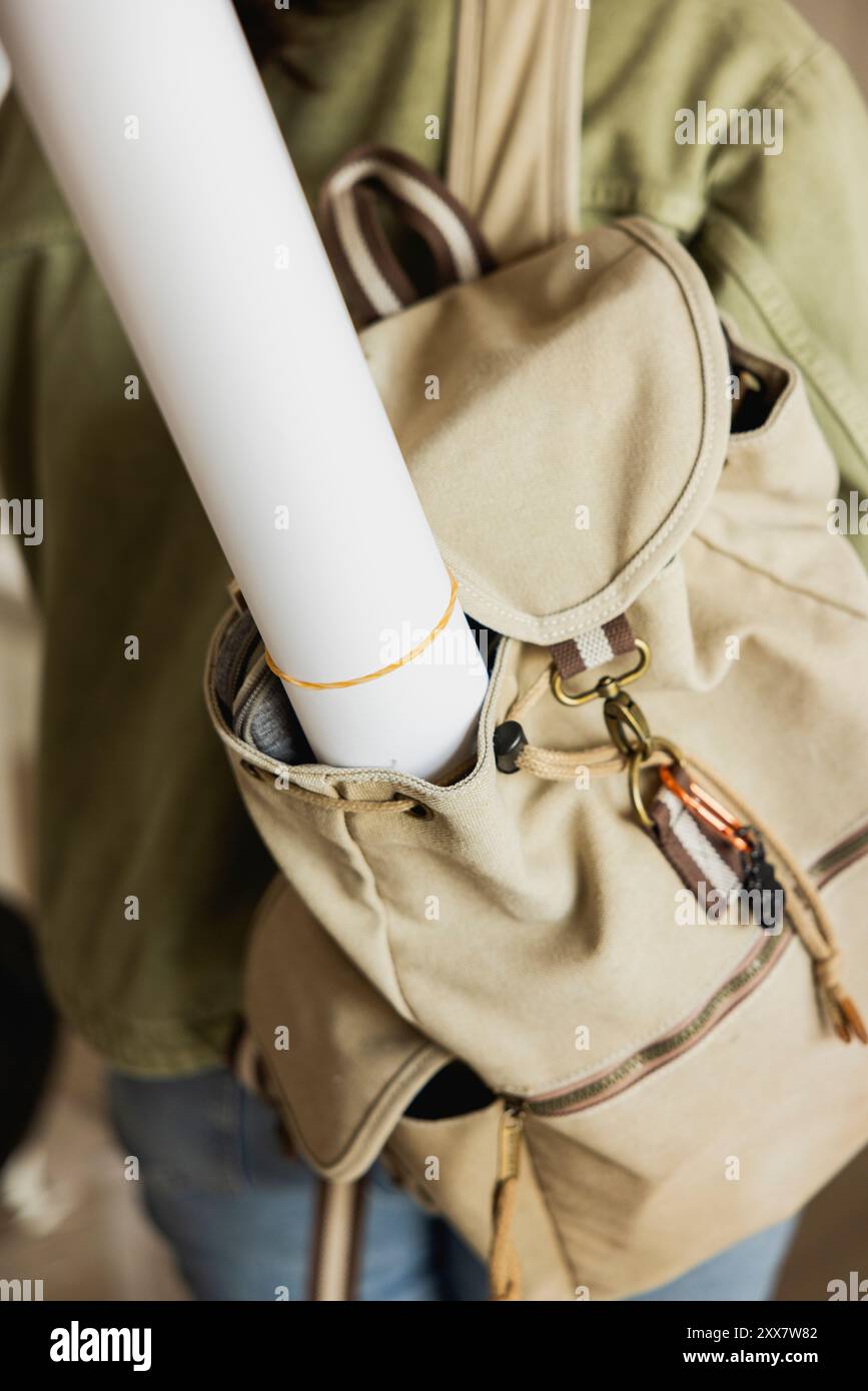 Rear view of a person carrying rolled-up poster in a beige backpack ...