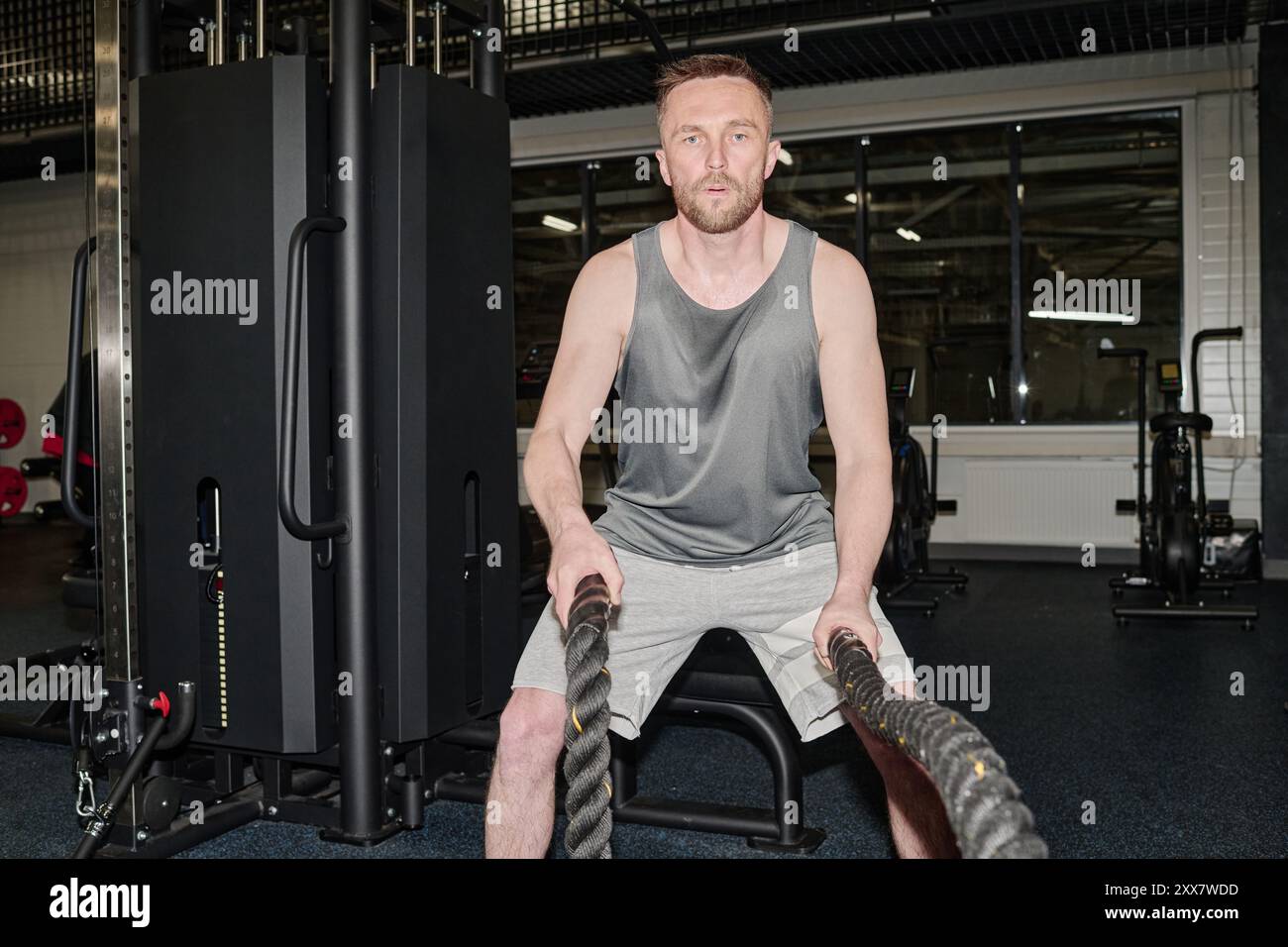 Tired man working out with battle ropes to develop arm and core muscles ...