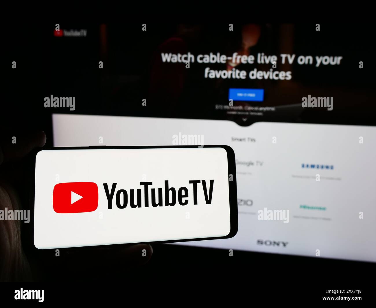 Person holding smartphone with logo of US IPTV service YouTube TV in front of website. Focus on ...