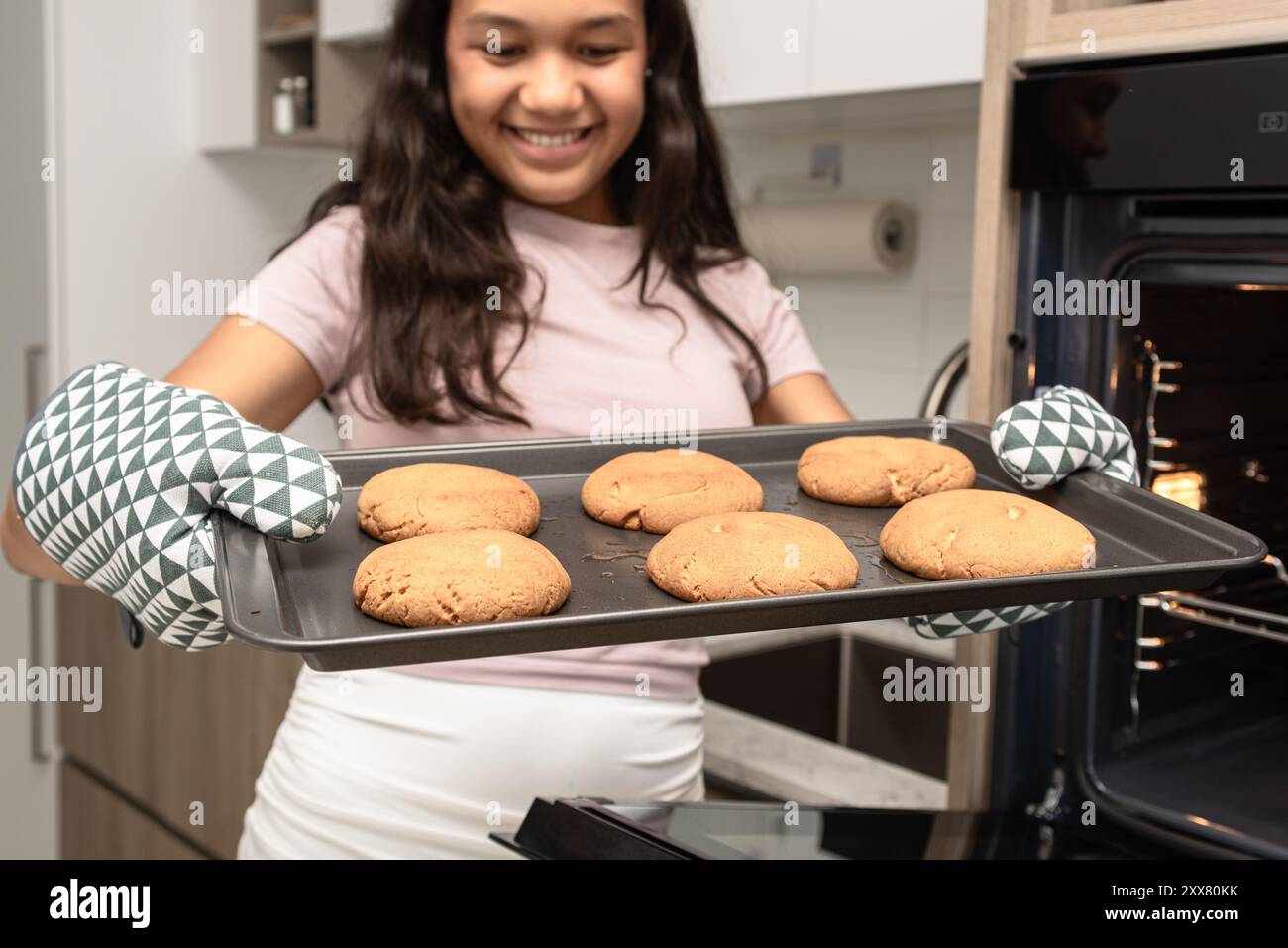 Smiling girl taking freshly baked cookies out of the oven Stock Photo ...