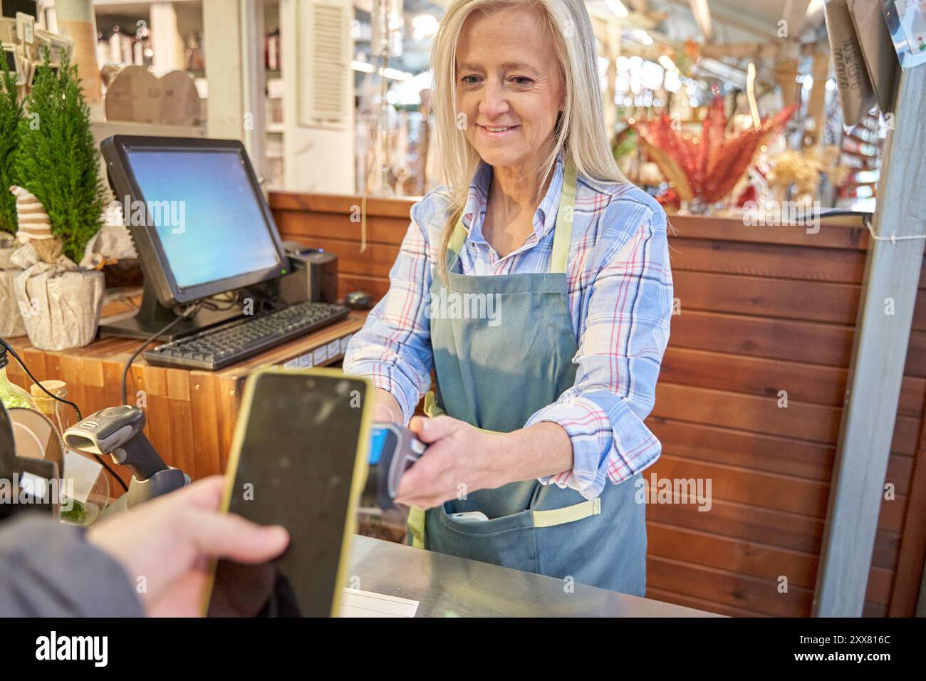 contactless mobile phone payment in a shop. middle-aged woman working ...