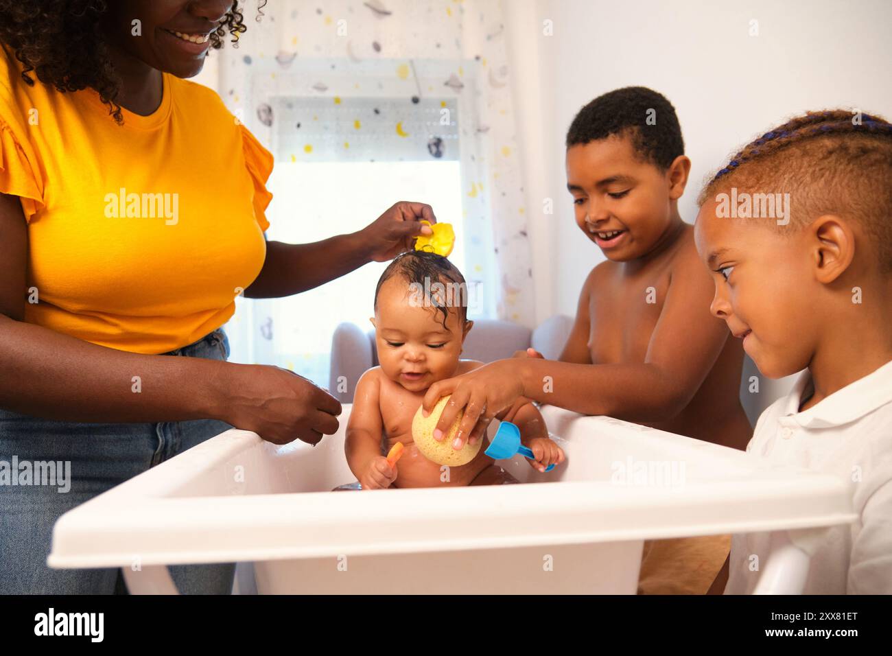 Mother washing baby in small bathtub helped by sons Stock Photo - Alamy