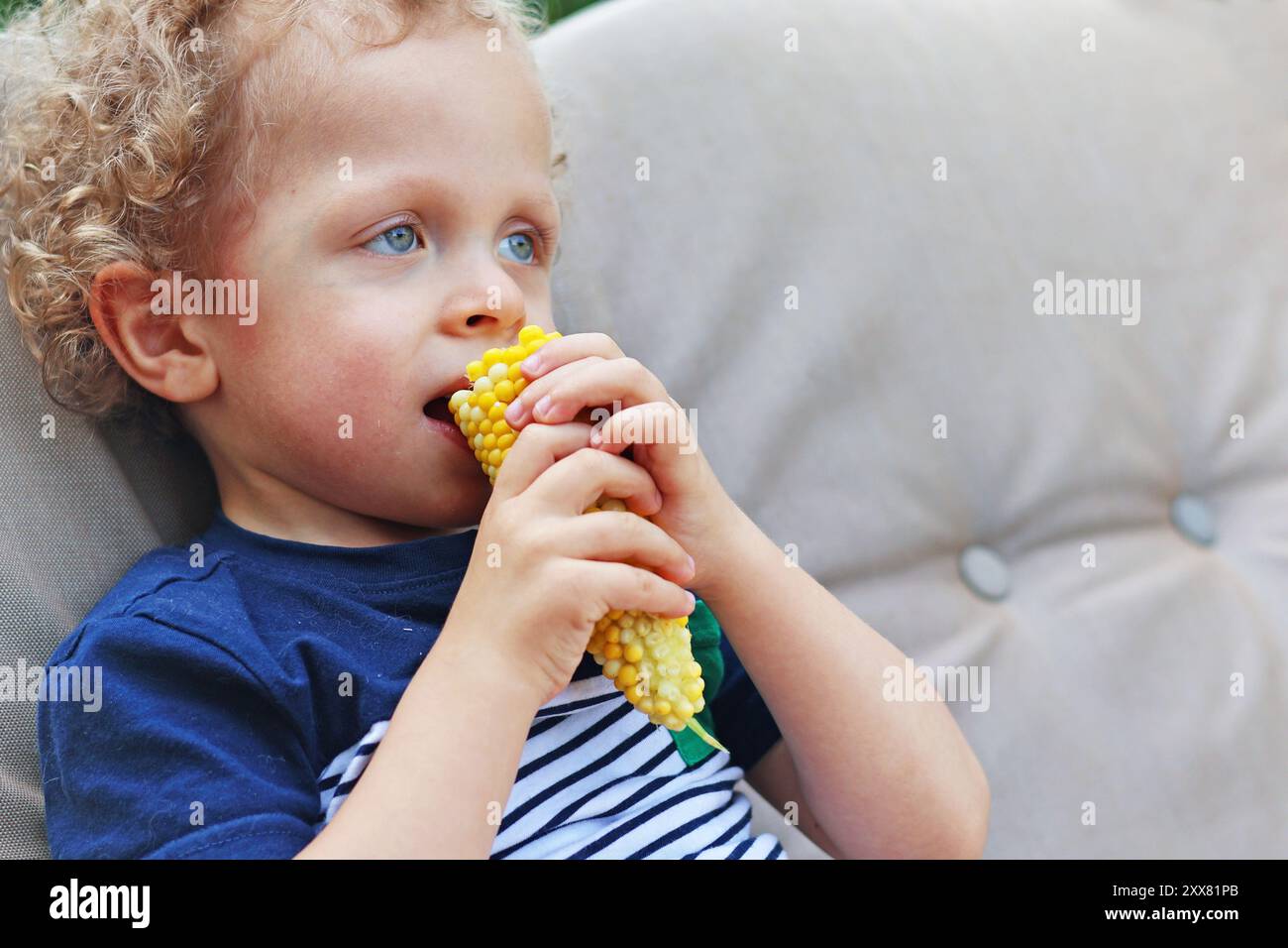 Little boy with blue eyes and curly hair eats corn Stock Photo - Alamy
