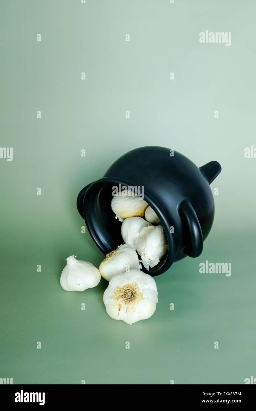 Garlic Spilling Out of Black Cauldron on Green Backdrop Stock Photo - Alamy