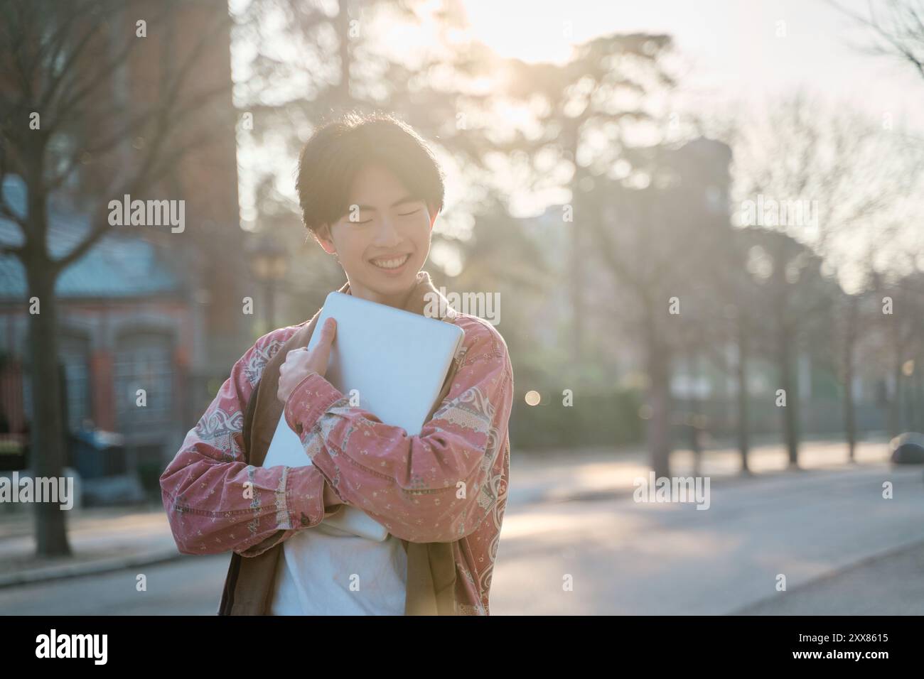 portrait of a young smiling student, hugging his laptop computer after ...