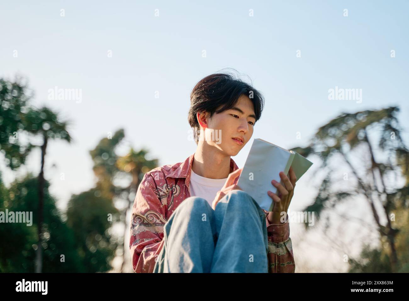 Chilling and focused young Asian male college student reading a book in ...