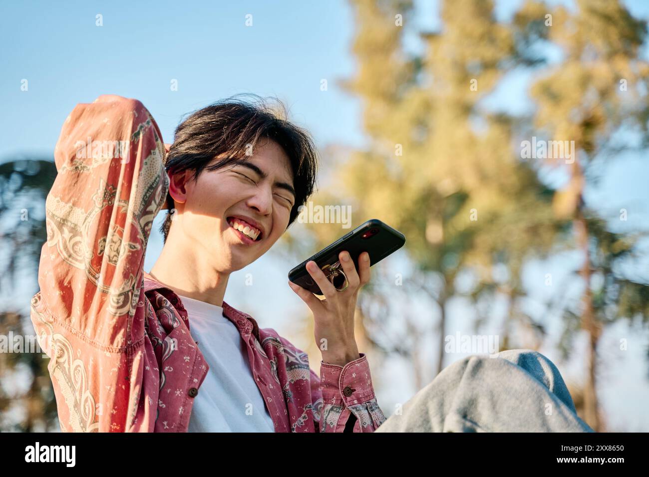 Happy asian man smiling using voice recognition on mobile phone in ...