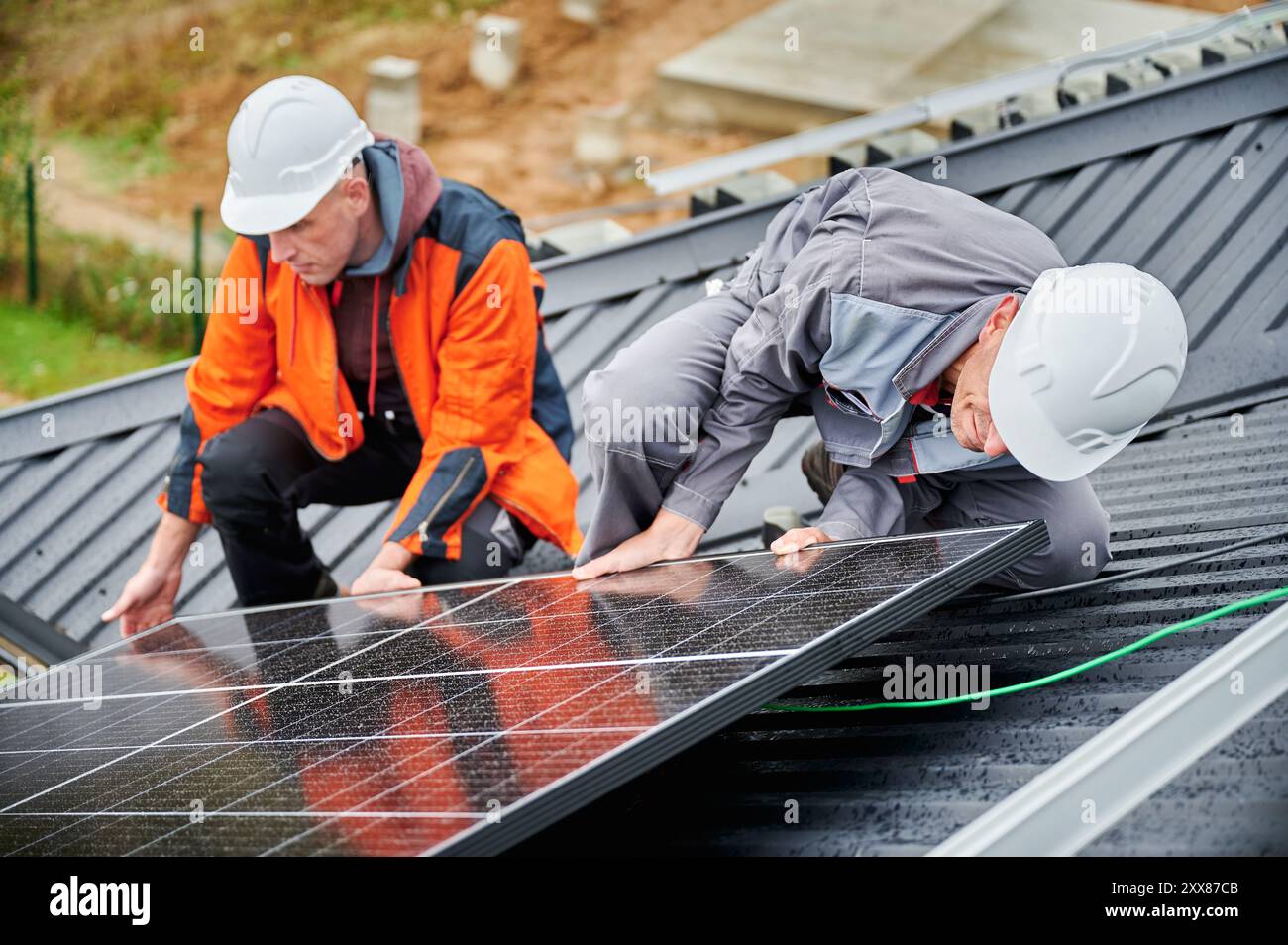 Workers building photovoltaic solar module station on roof of house ...