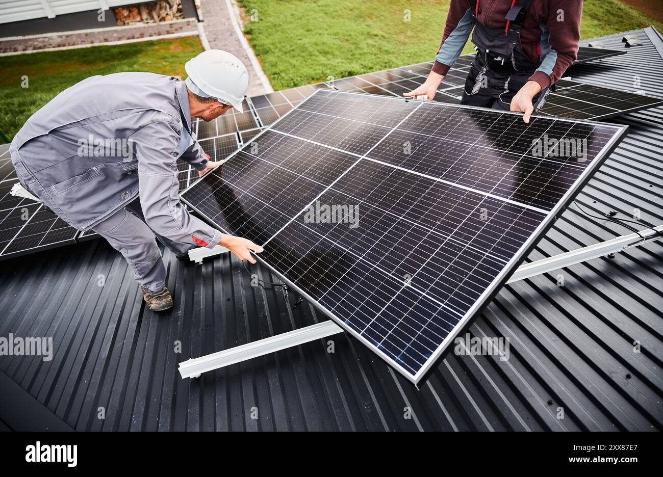 Technicians installing solar panel system on roof of house. Men Installers in helmets carrying ...
