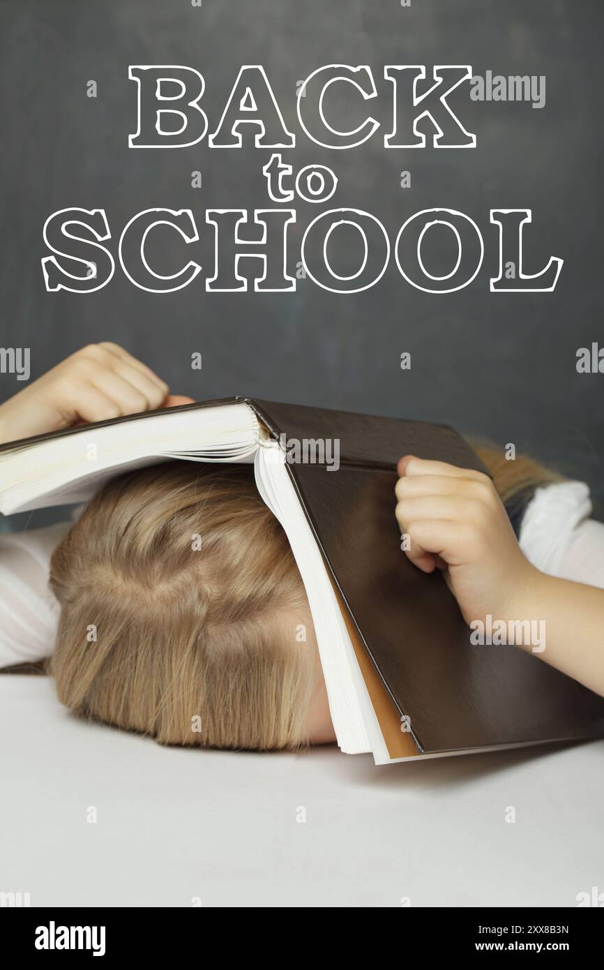 Little child girl pupil hiding under textbook in classroom against ...